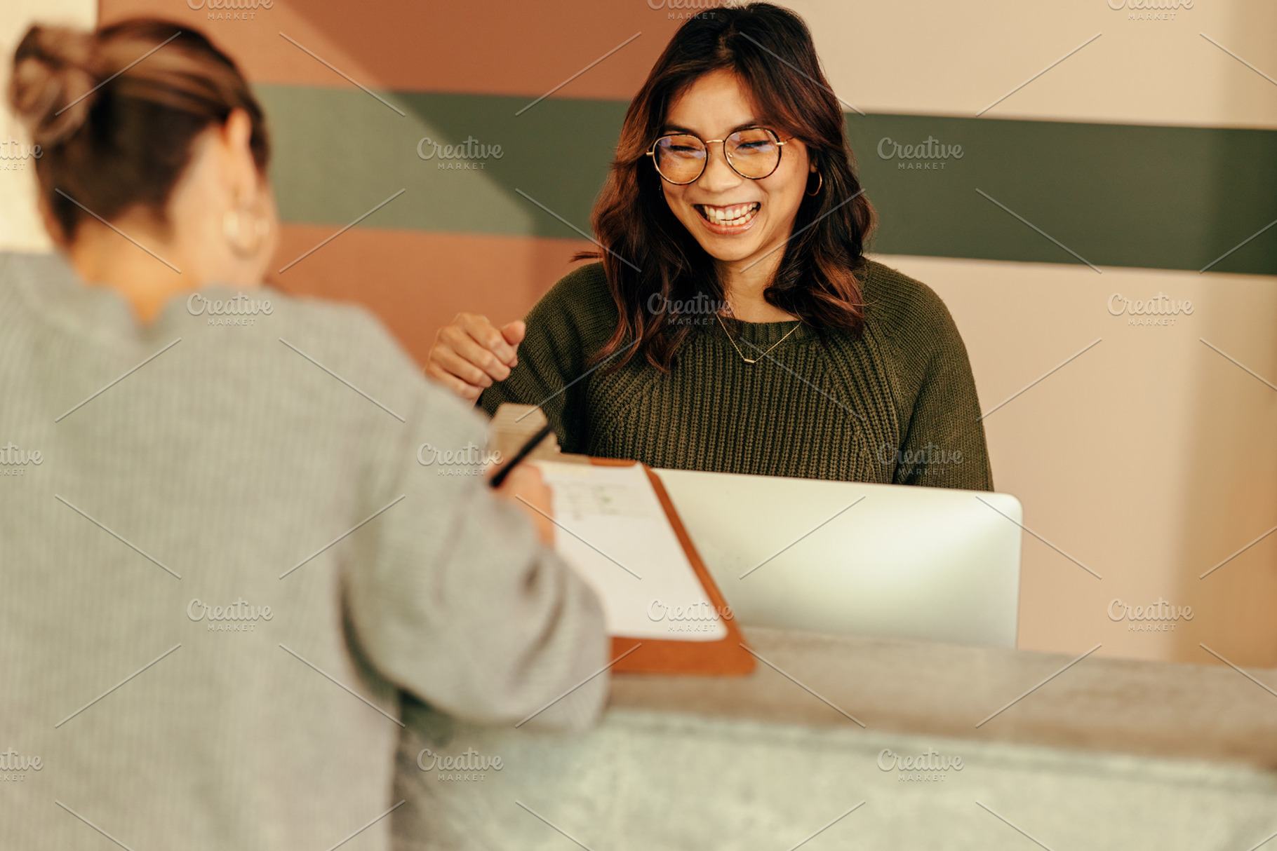 Cheerful receptionist assisting a woman with signing in to an of, a ...