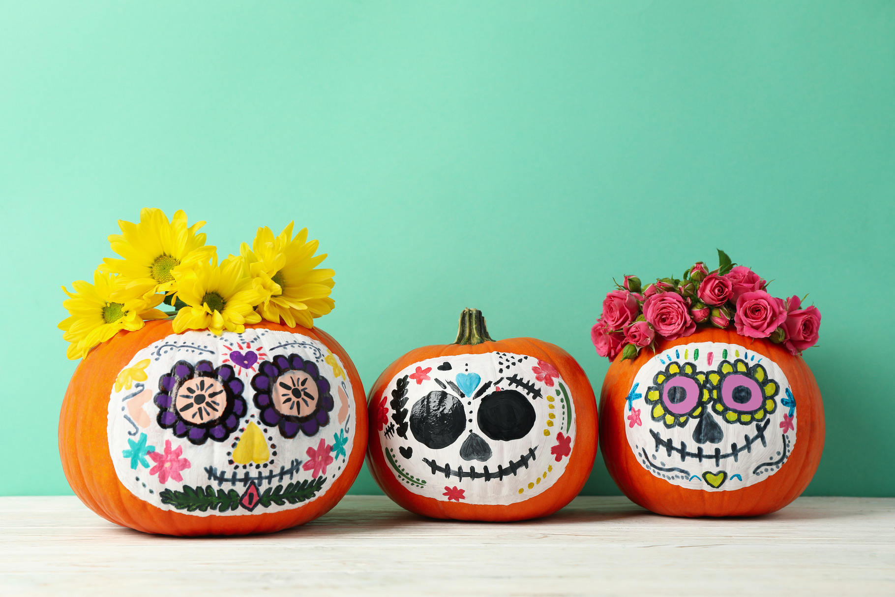 Pumpkins with catrina skull makeup and flowers on mint backgroun, a ...