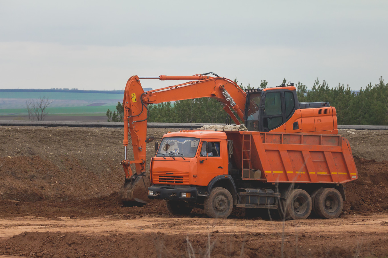 Heavy excavator loading dumper truck on road construction among fields ...