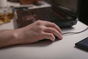 Male hand holding computer mouse with laptop keyboard in the background ...