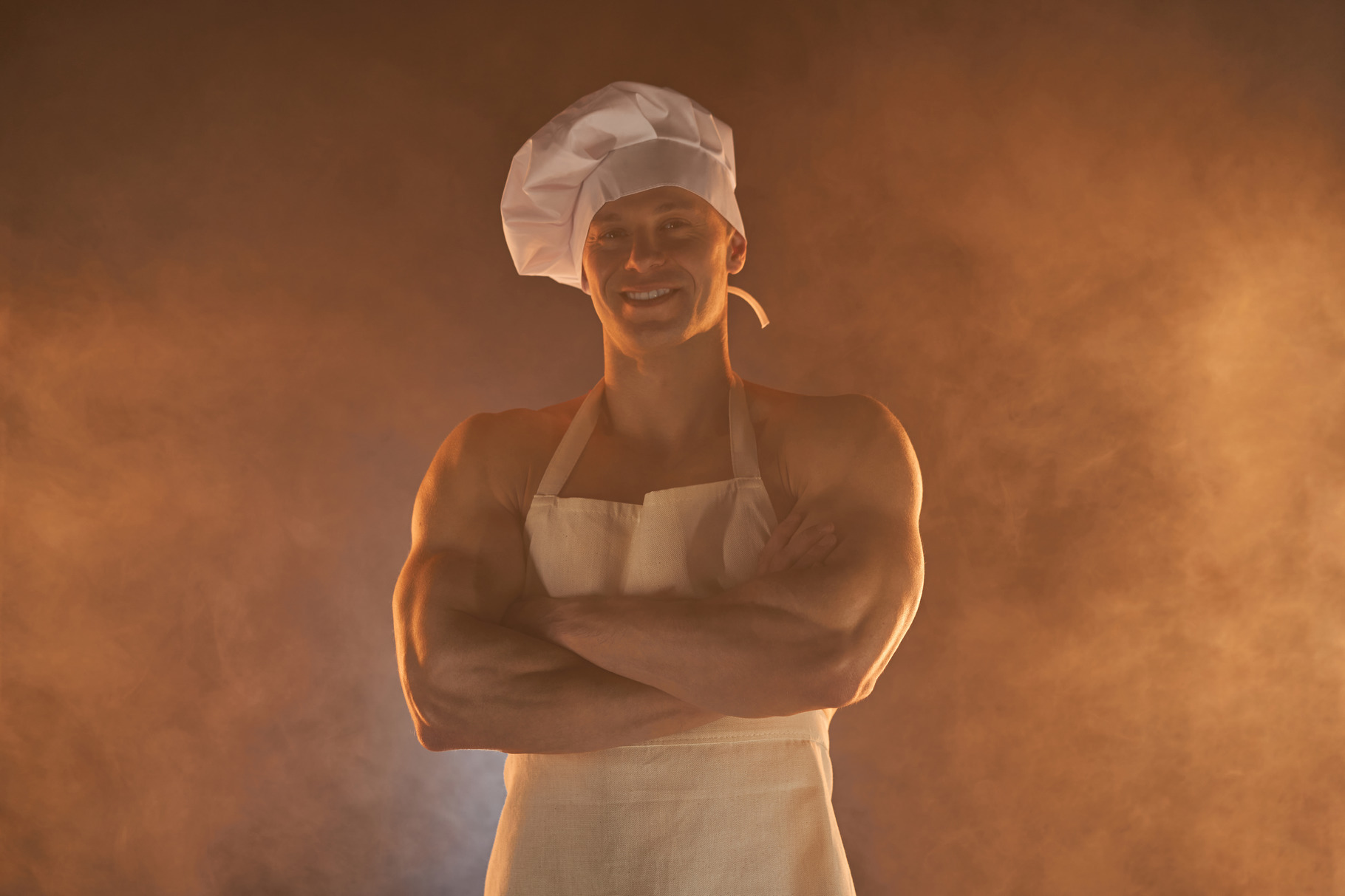 Portrait of muscular chef wearing white apron and chef hat, posing with ...