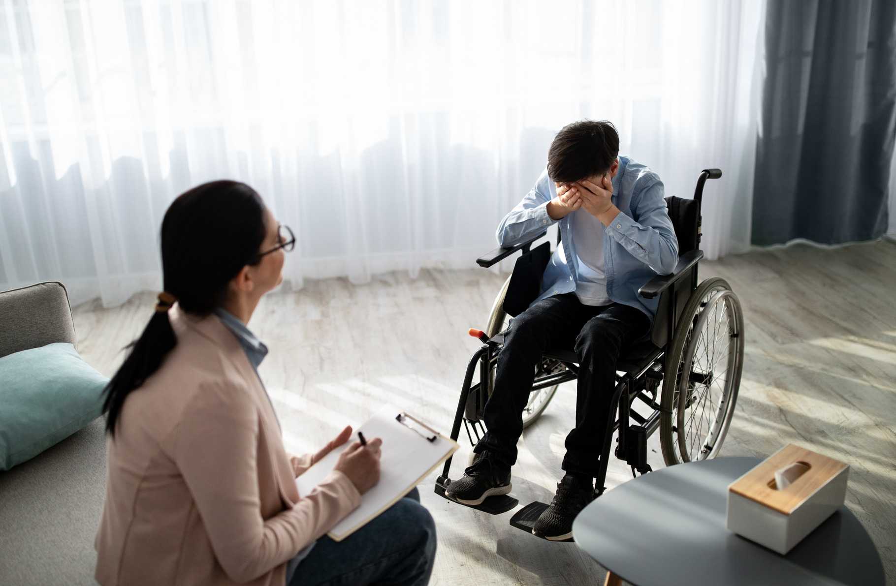 Above view of handicapped teen boy in wheelchair crying on consultation ...