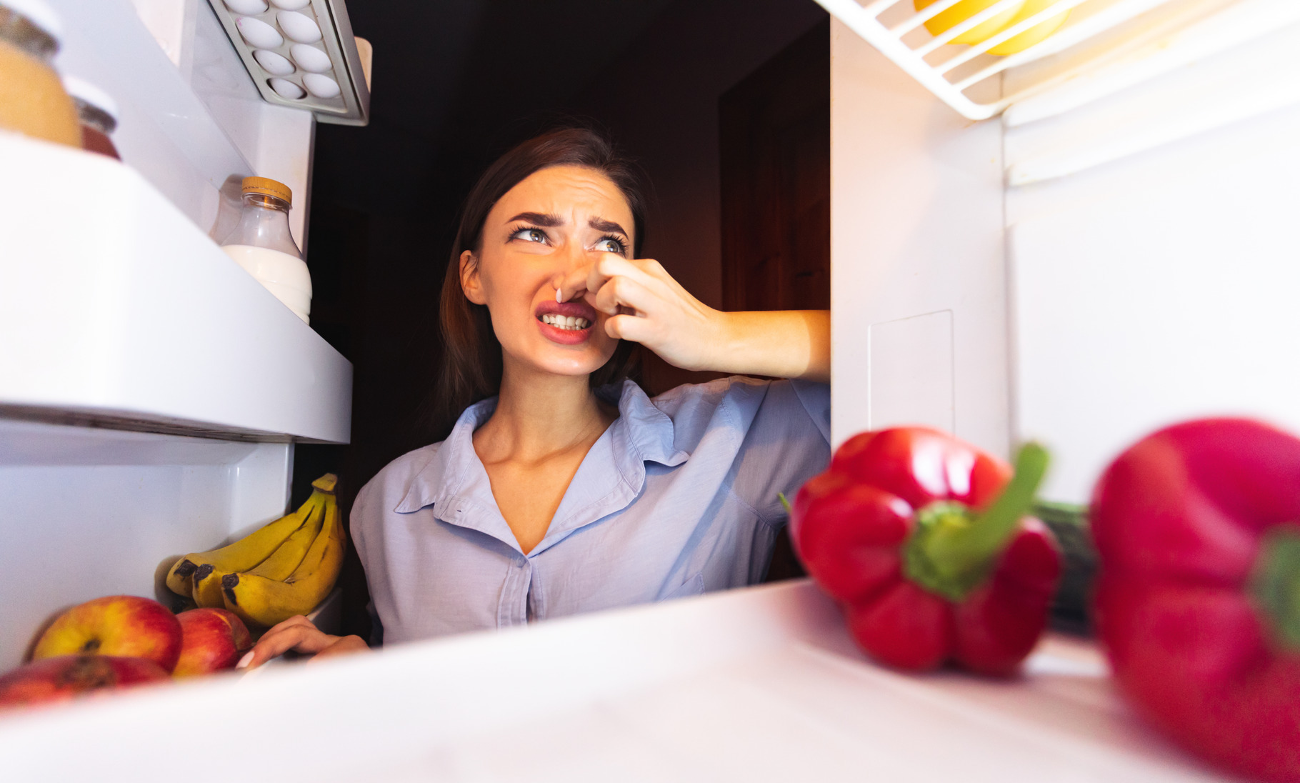 Woman closing nose near refrigerator, a Photo by Prostock-Studio