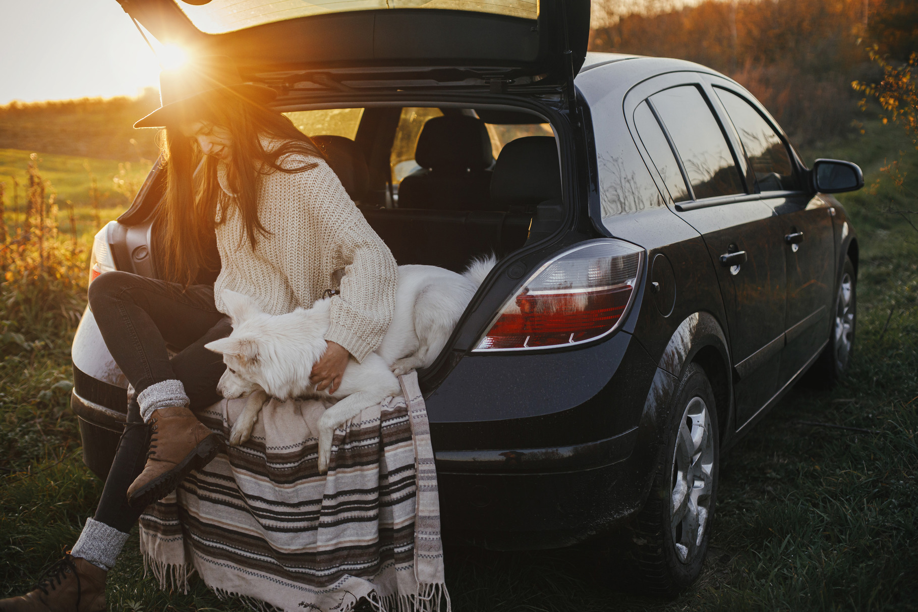 Stylish woman sitting and hugging cute dog in car trunk in sunse, a ...