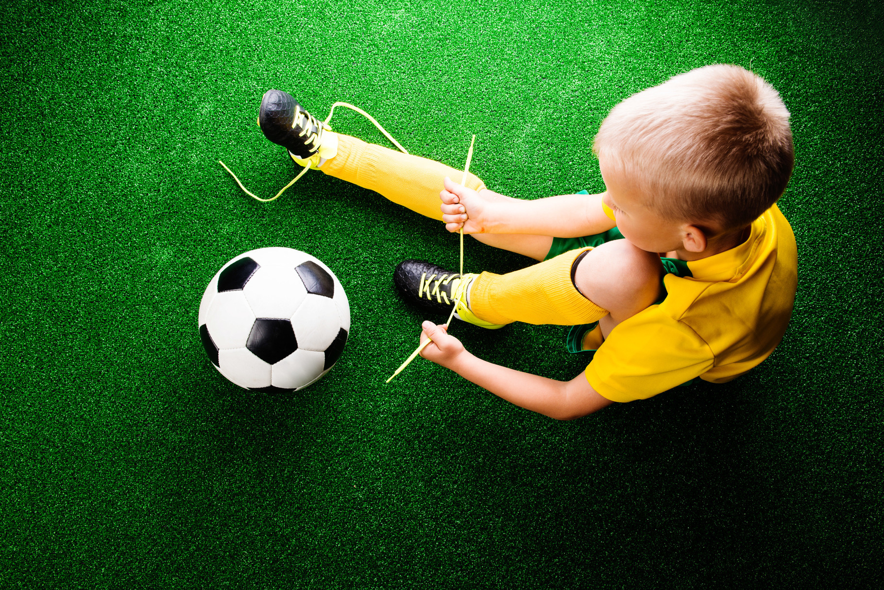 Unrecognizable little football player against green grass studi ...