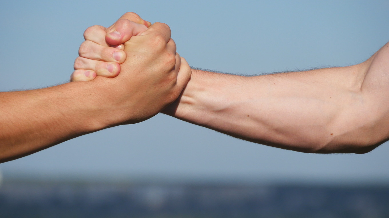 Friendly handshake of two unrecognizable muscular white men on blue sky ...