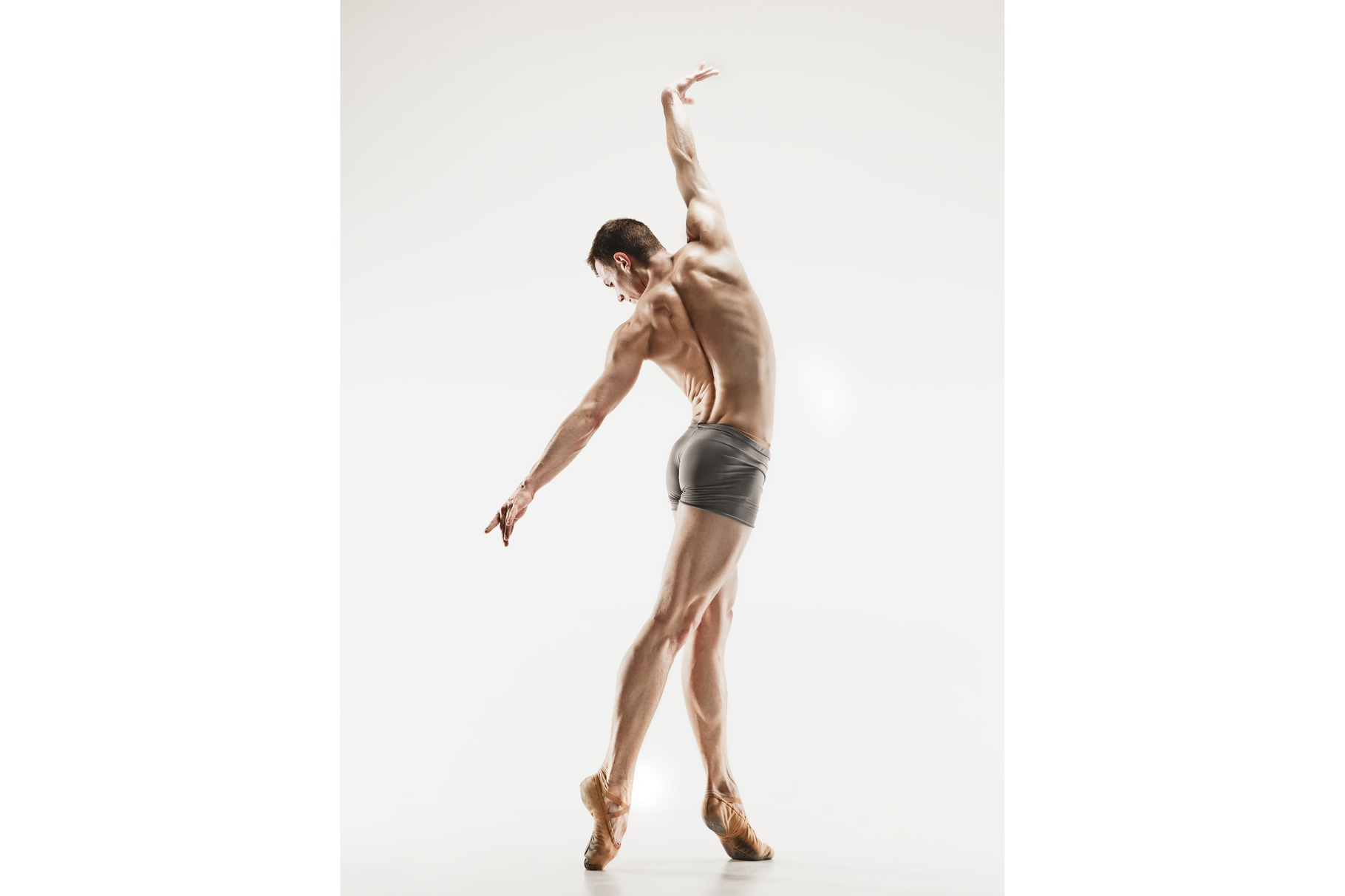 Athletic ballet dancer in a perfect shape performing over the grey ...