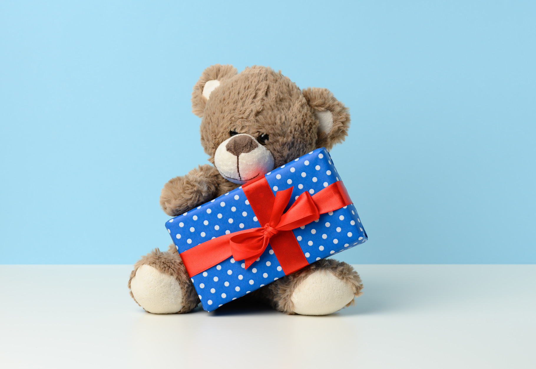 cute brown teddy bear holding a box wrapped in blue paper and re, a ...
