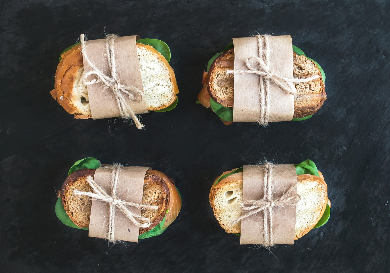 Sandwiches wrapped in craft paper containing dark, stone, and tost, a ...