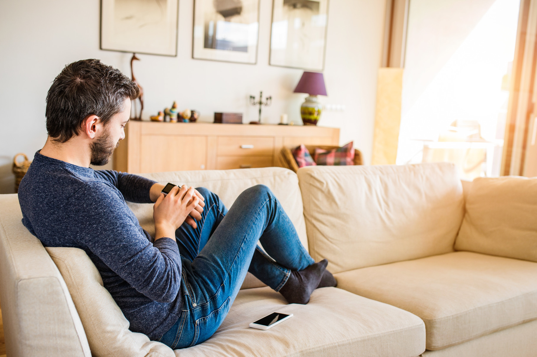 Man at home sitting on sofa using smart watch featuring screen, working ...